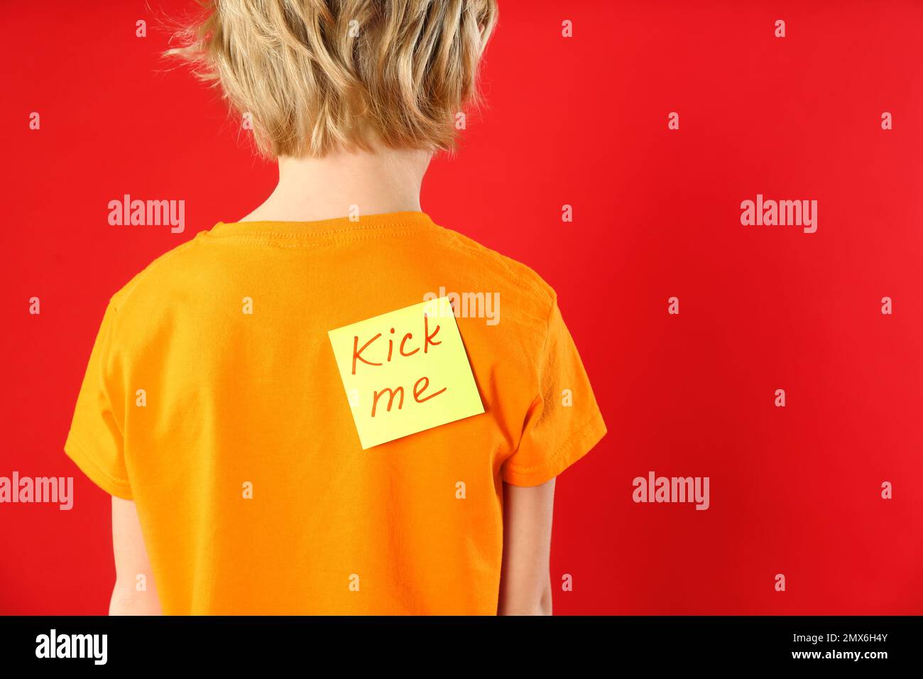 Little boy with KICK ME sticker on back against red background. April ...