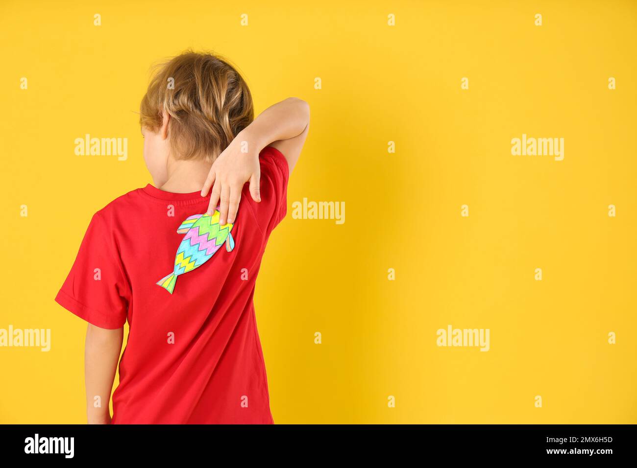 Little boy with paper fish on back against yellow background, space for ...