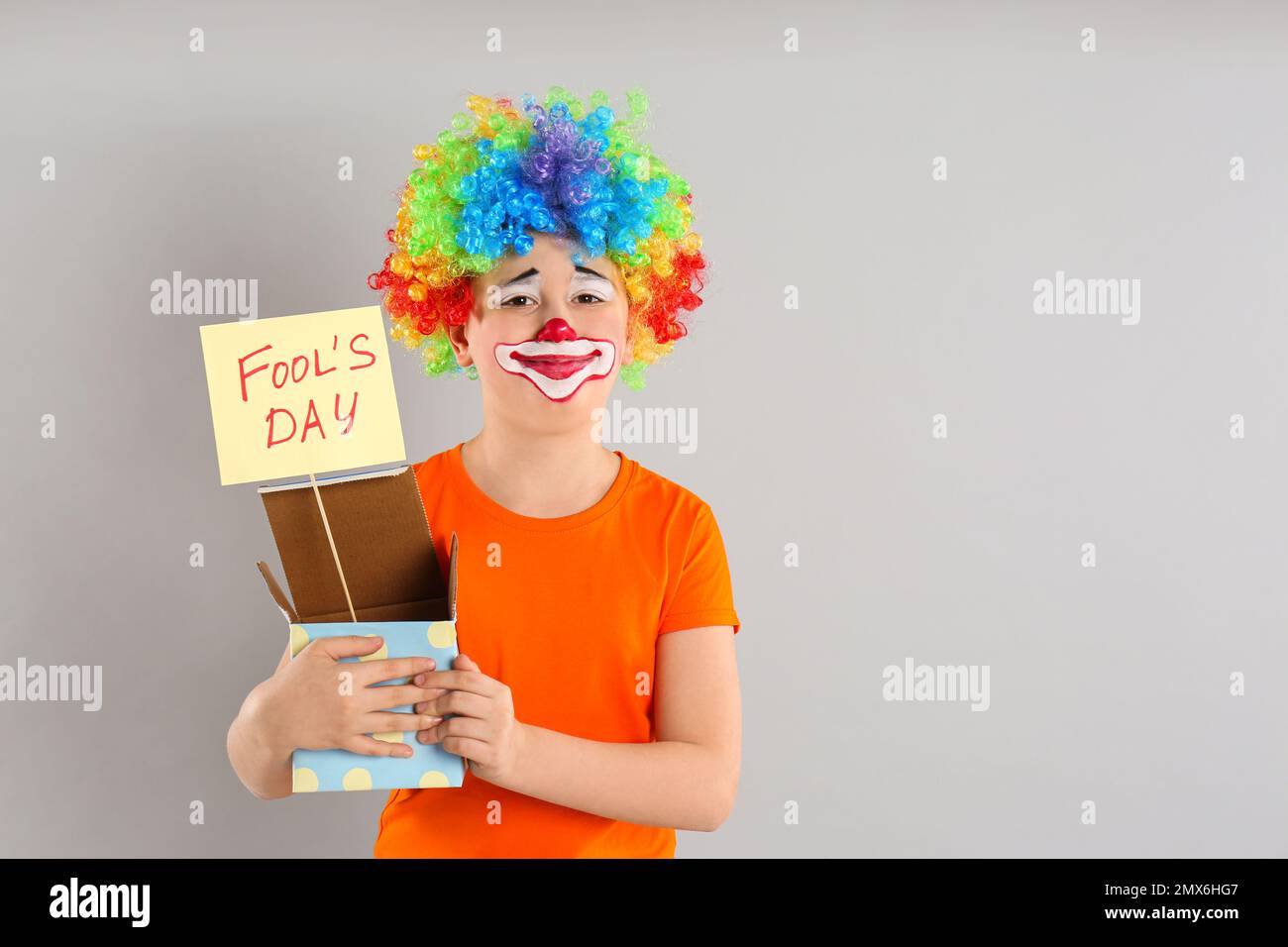Preteen boy with clown makeup and wig holding APRIL FOOL'S DAY sign on ...