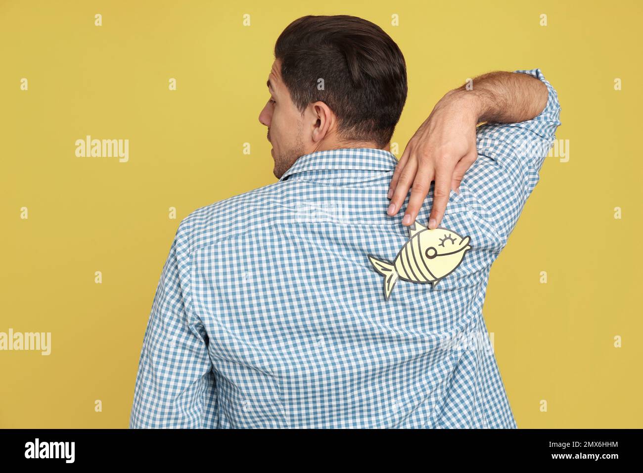 Man with paper fish on back against yellow background. April fool's day ...