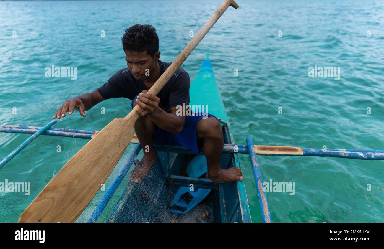 Young asian fisherman rowing while throwing fishing net at sea ...