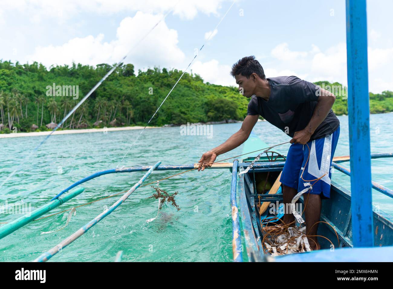 Asian fisherman picking up his fishing net on a small boat at sea with ...