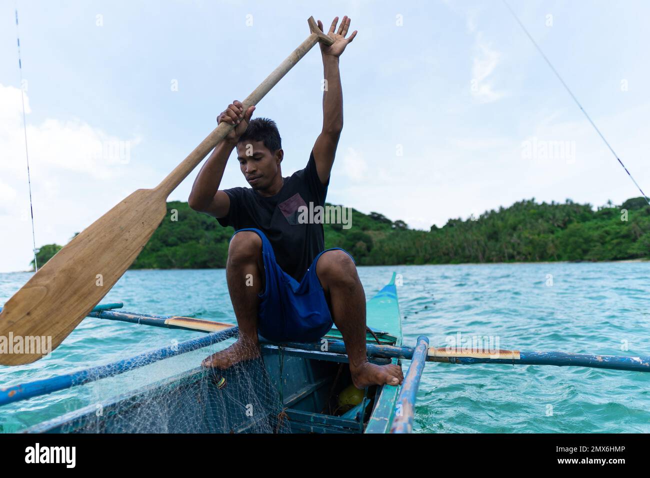 Young asian fisherman rowing while throwing fishing net at sea ...