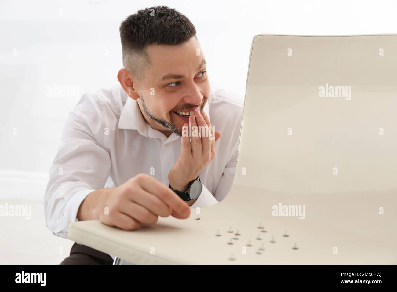 Man putting pins on chair in office. April fool's day Stock Photo - Alamy