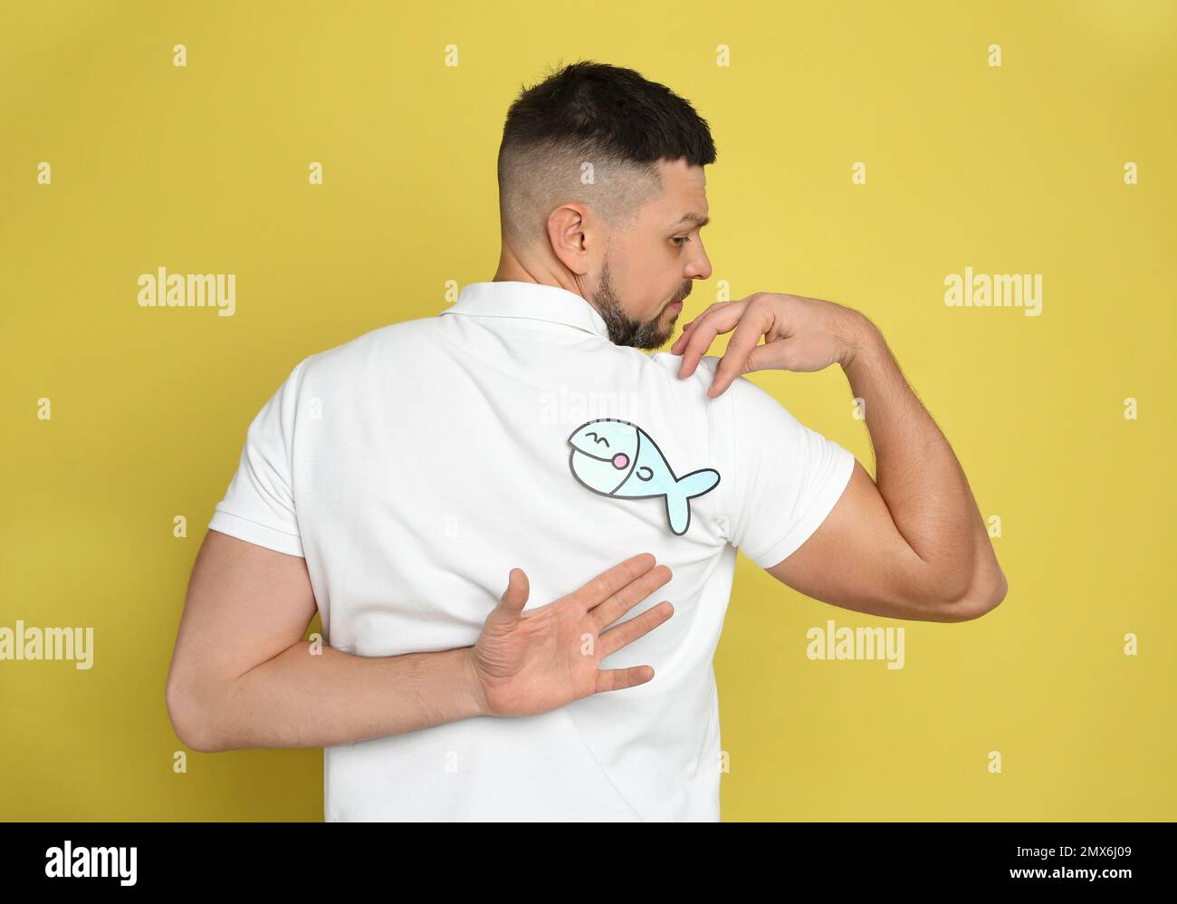 Man with paper fish on back against yellow background. April fool's day ...