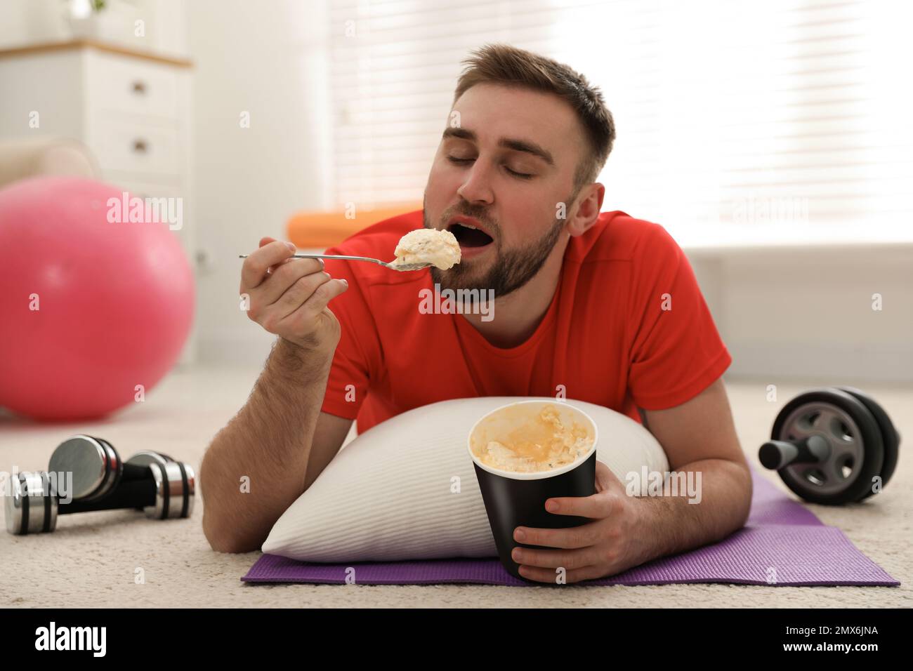 Lazy young man eating ice cream instead of training at home Stock Photo ...
