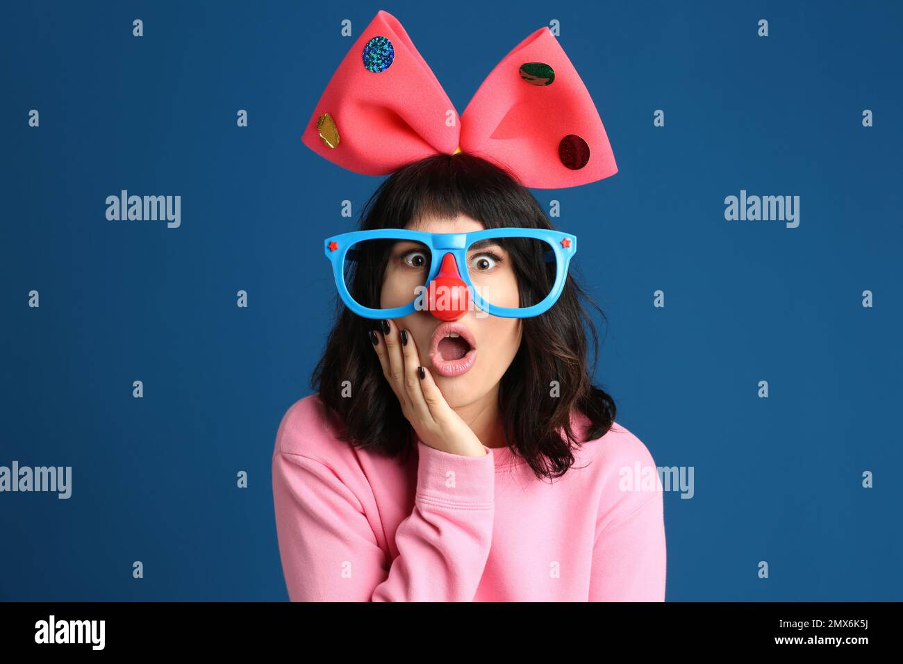 Emotional woman with funny glasses and large bow on blue background ...