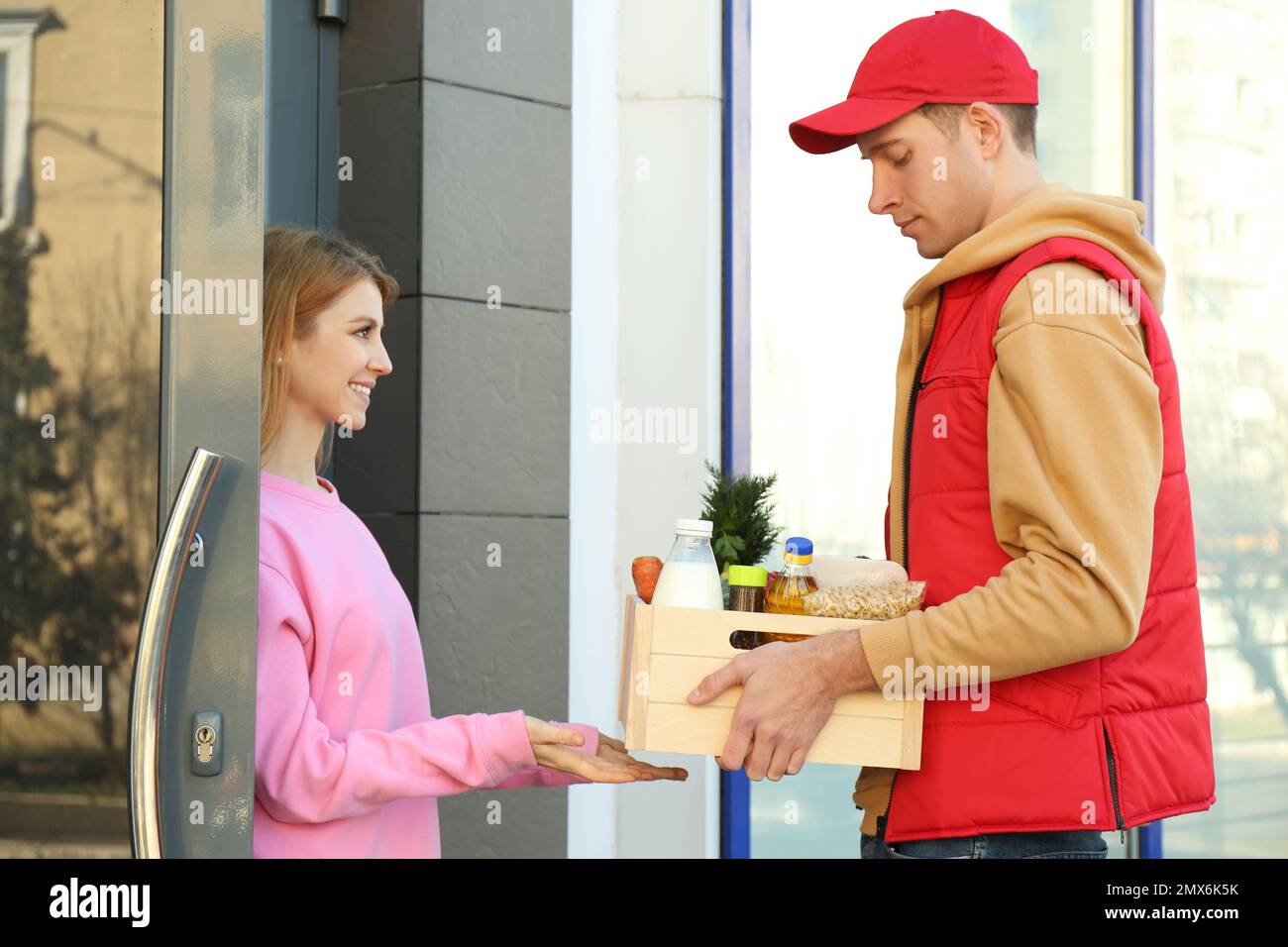 Woman receiving fresh products from courier at entrance. Food delivery ...