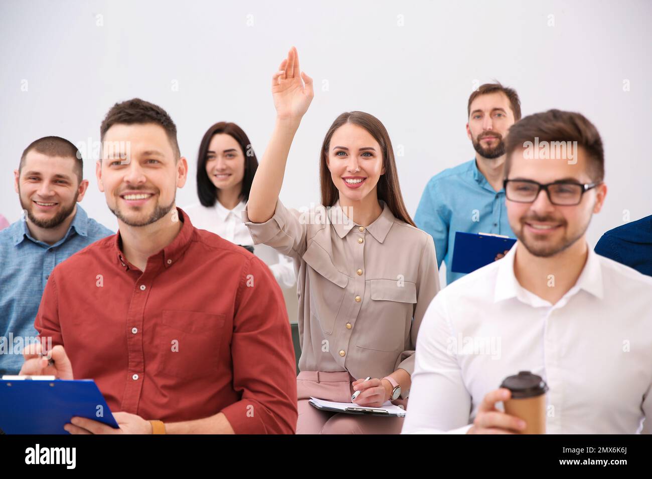 Young woman raising hand to ask question at business training on white ...
