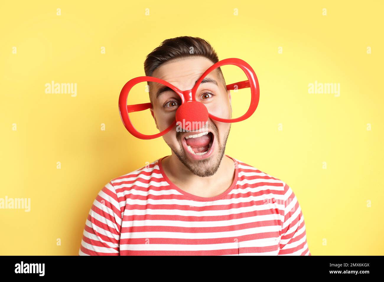 Emotional young man with party glasses and clown nose on yellow ...