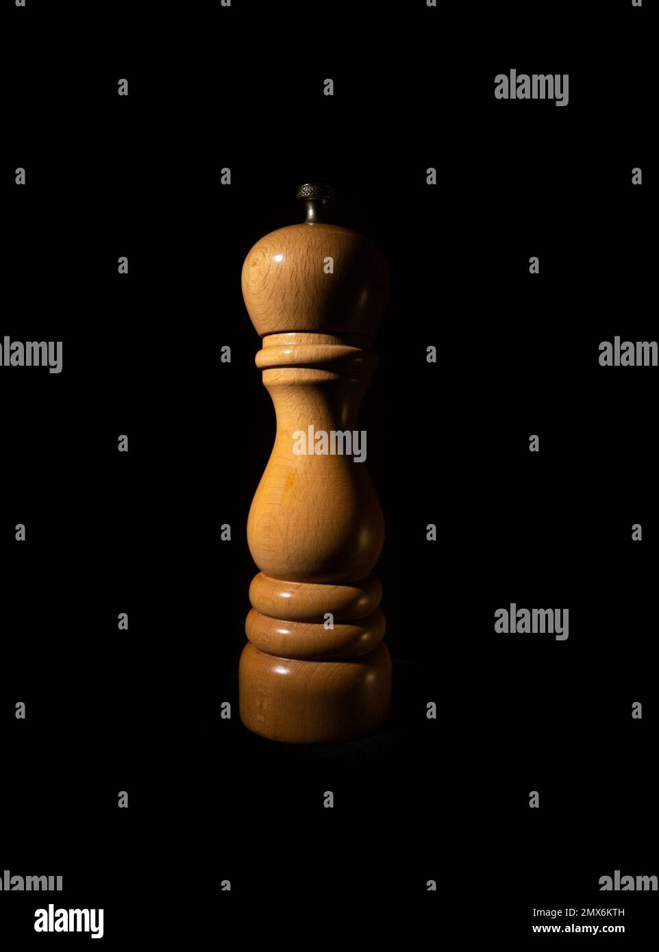 Wooden hourglass shaped manual pepper mill against a black background ...