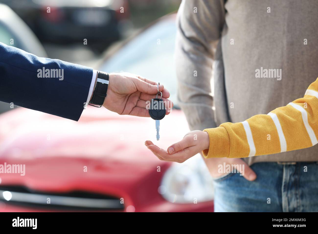Salesman giving key to customers in modern auto dealership, closeup ...