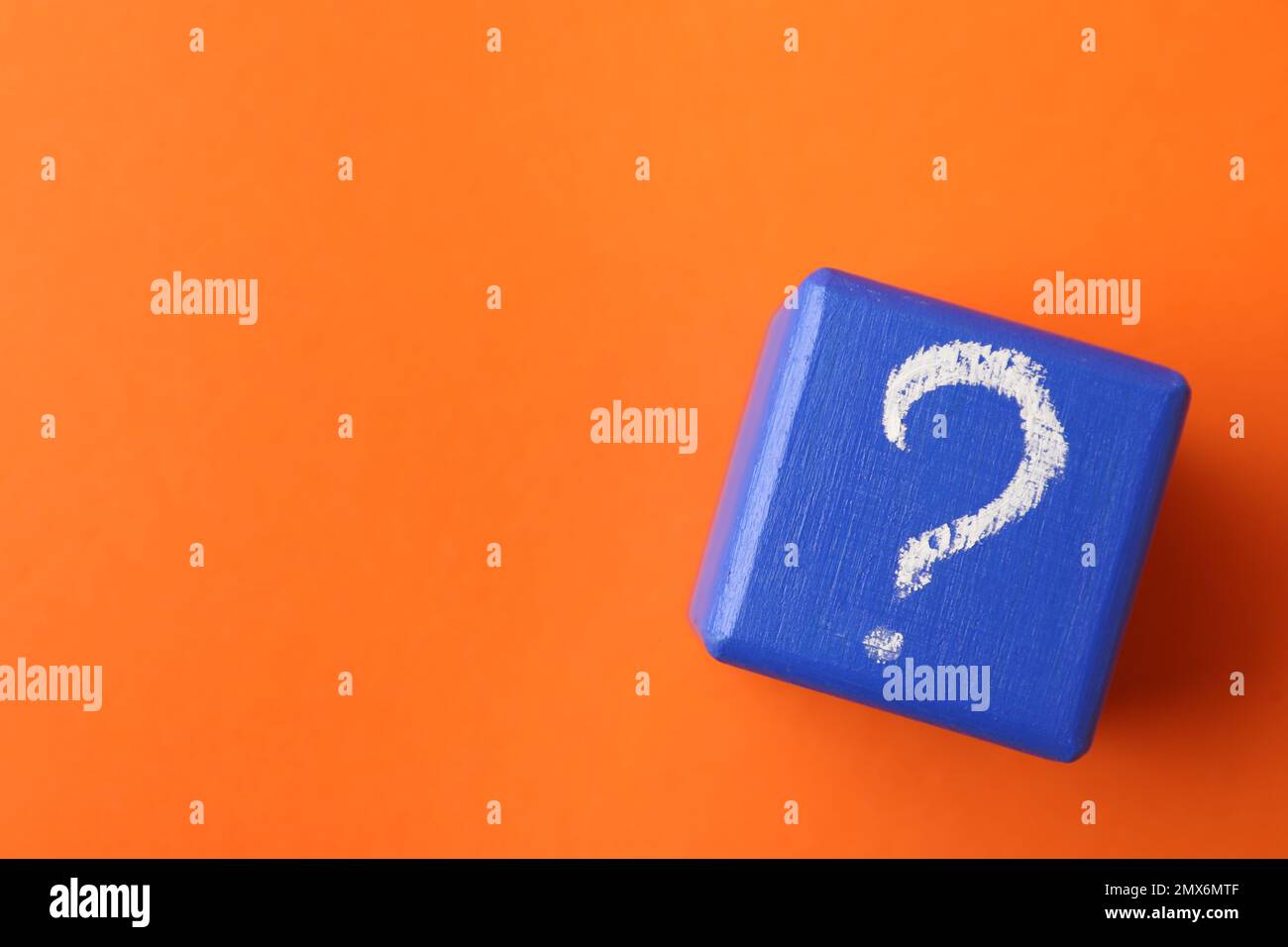 Blue wooden cube with question mark on orange background, top view ...