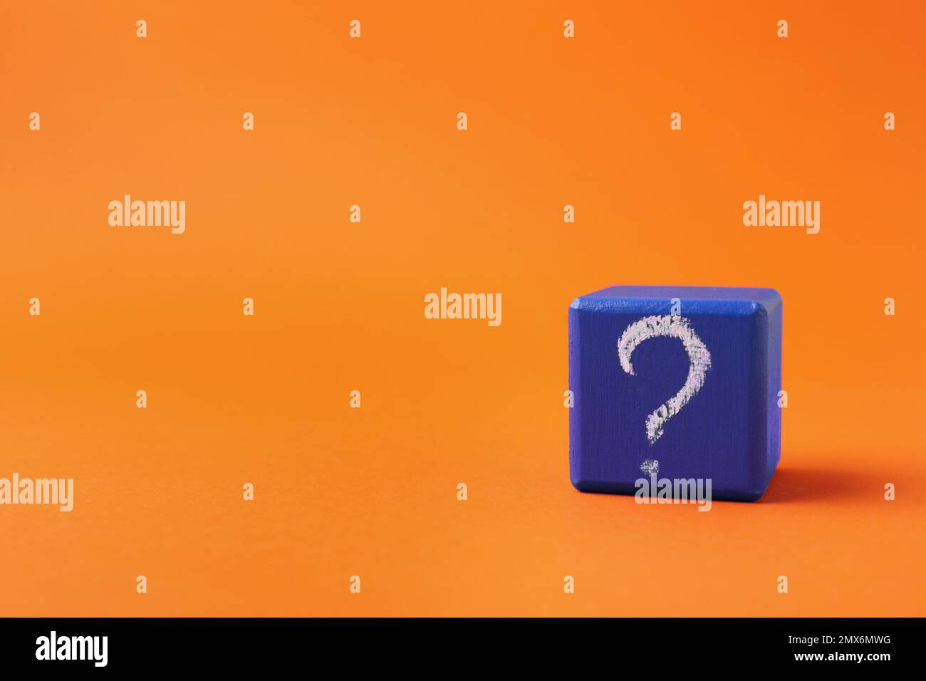 Blue wooden cube with question mark on orange background. Space for ...