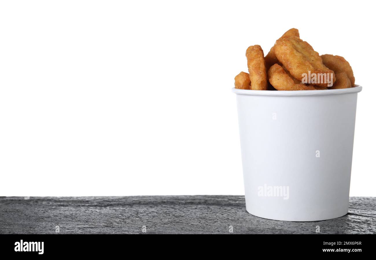 Bucket with tasty chicken nuggets on grey table against white ...