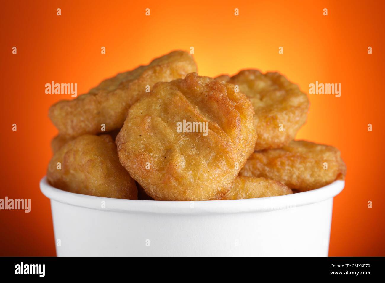 Bucket with delicious chicken nuggets on orange background, closeup ...