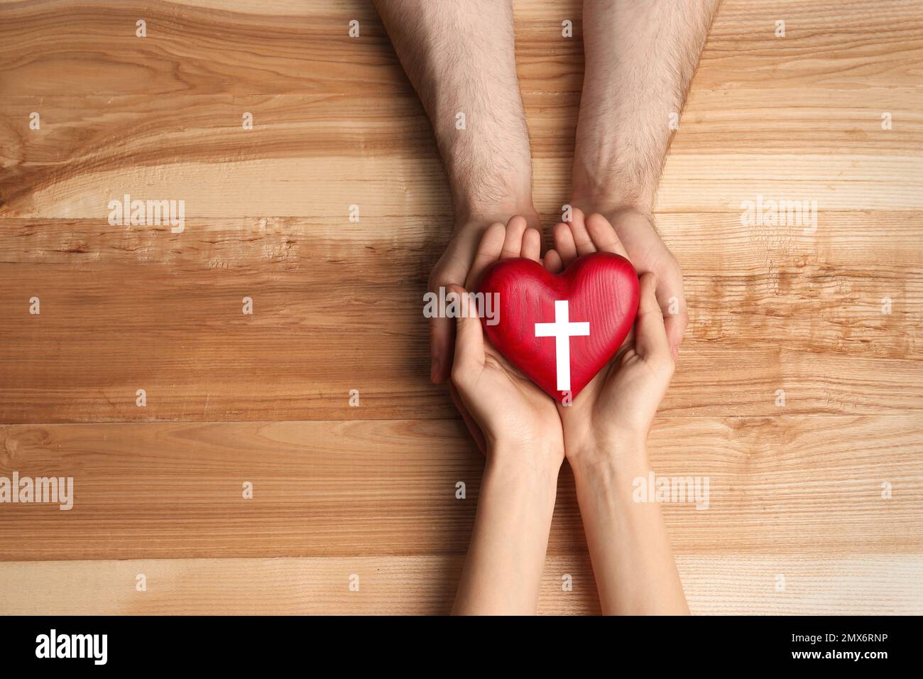 Couple holding heart with cross symbol on wooden background, top view ...