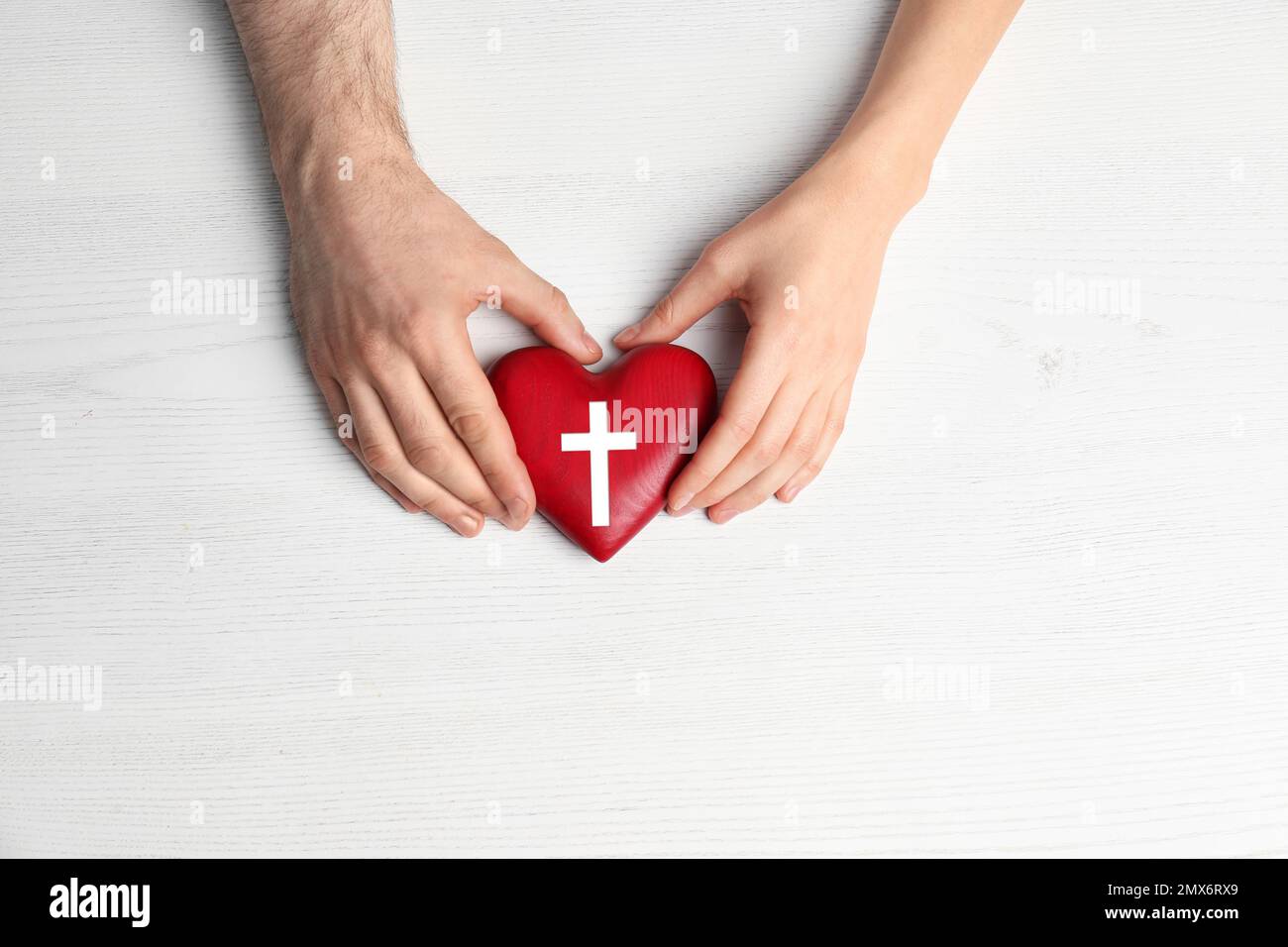 Couple holding heart with cross symbol on white wooden background, top ...