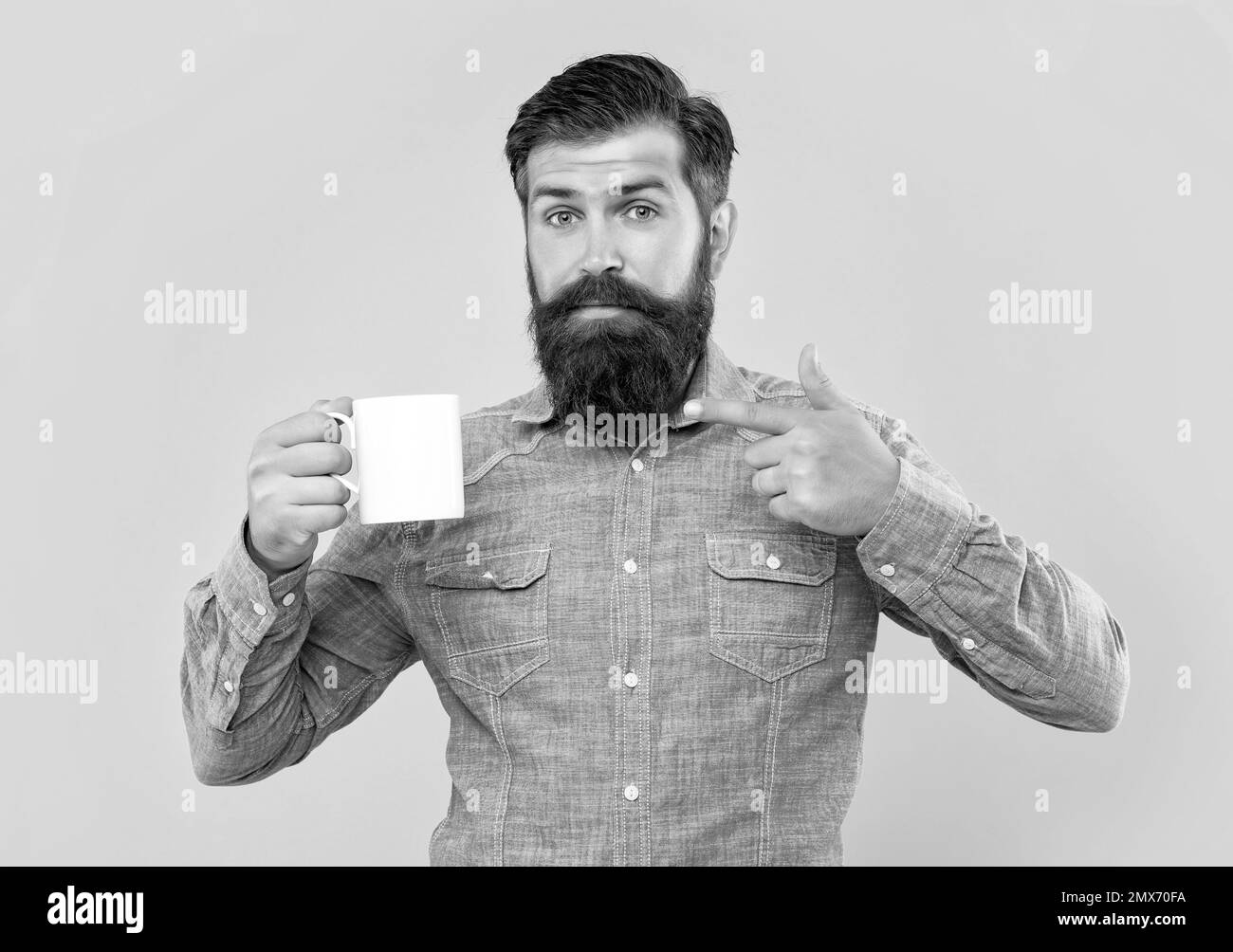 Serious man pointing finger at coffee mug yellow background, copy space ...