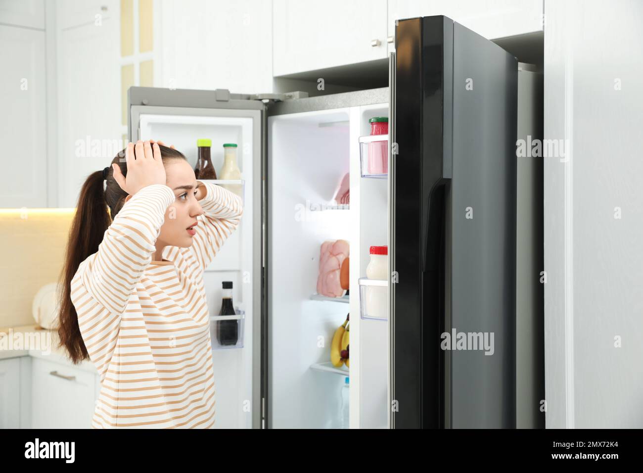 Emotional young woman near open refrigerator in kitchen Stock Photo - Alamy