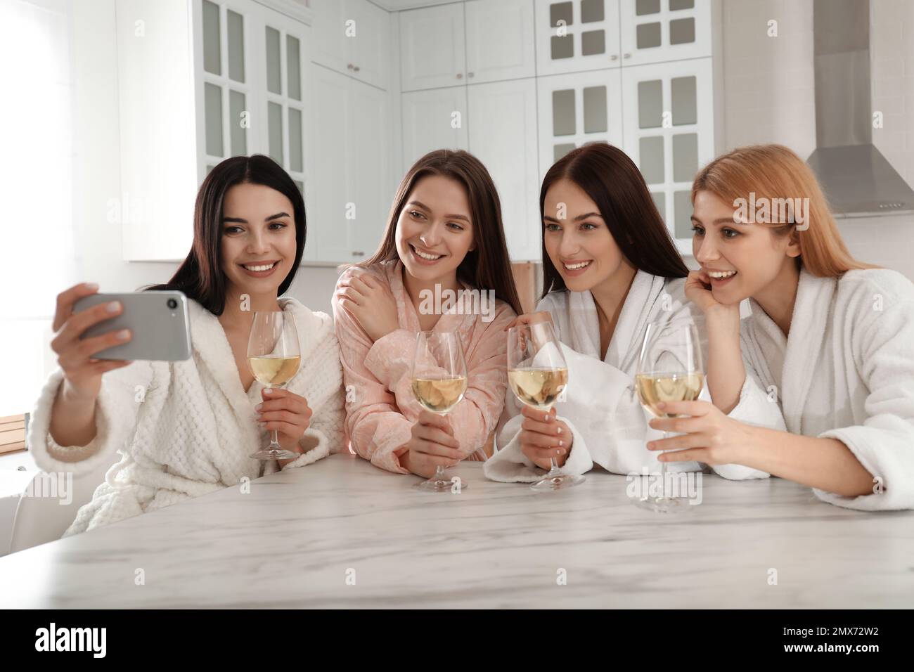 Beautiful young ladies with wine taking selfie in kitchen at pamper ...