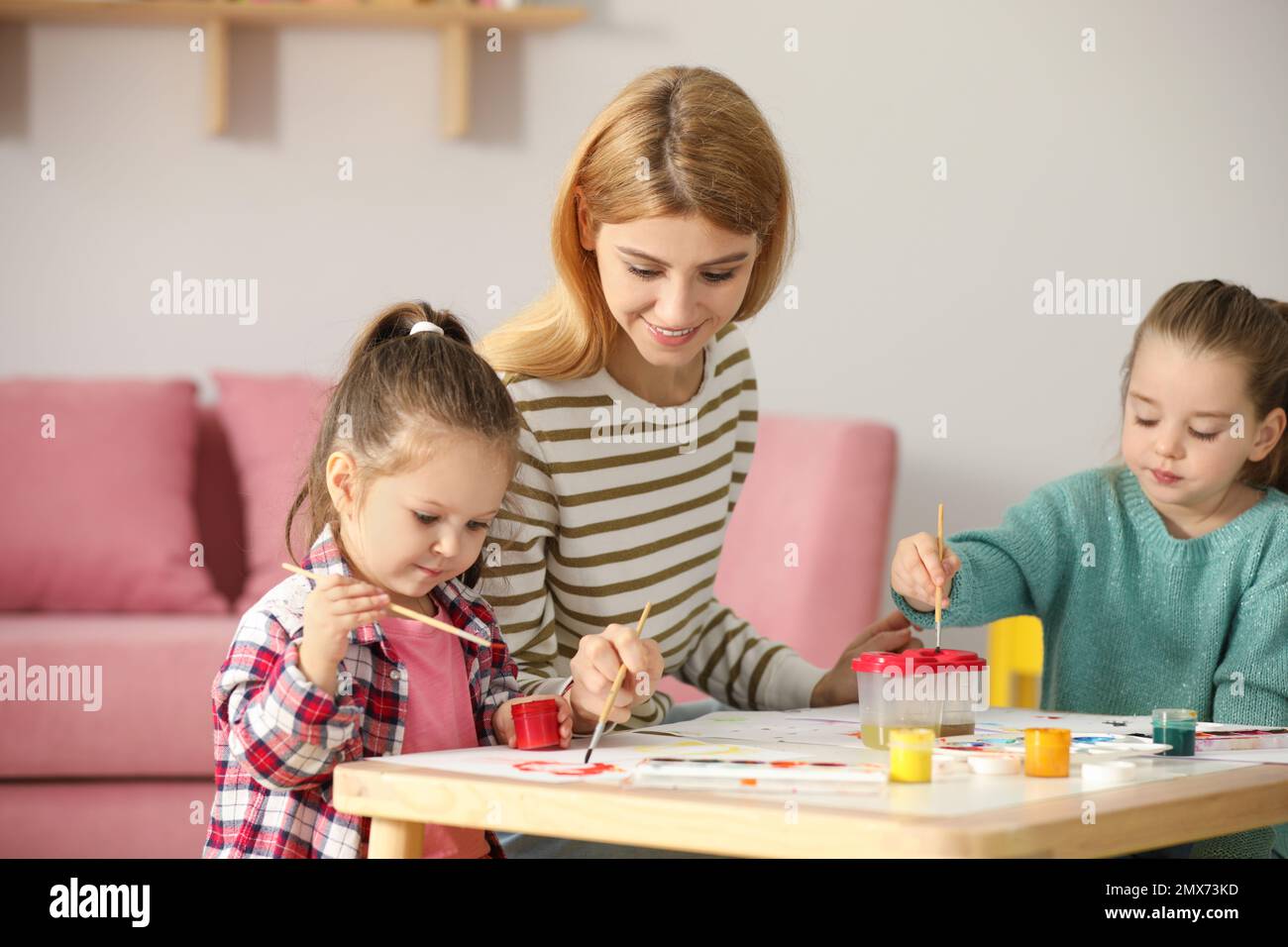 Mother and daughters painting at table indoors. Playing with children ...