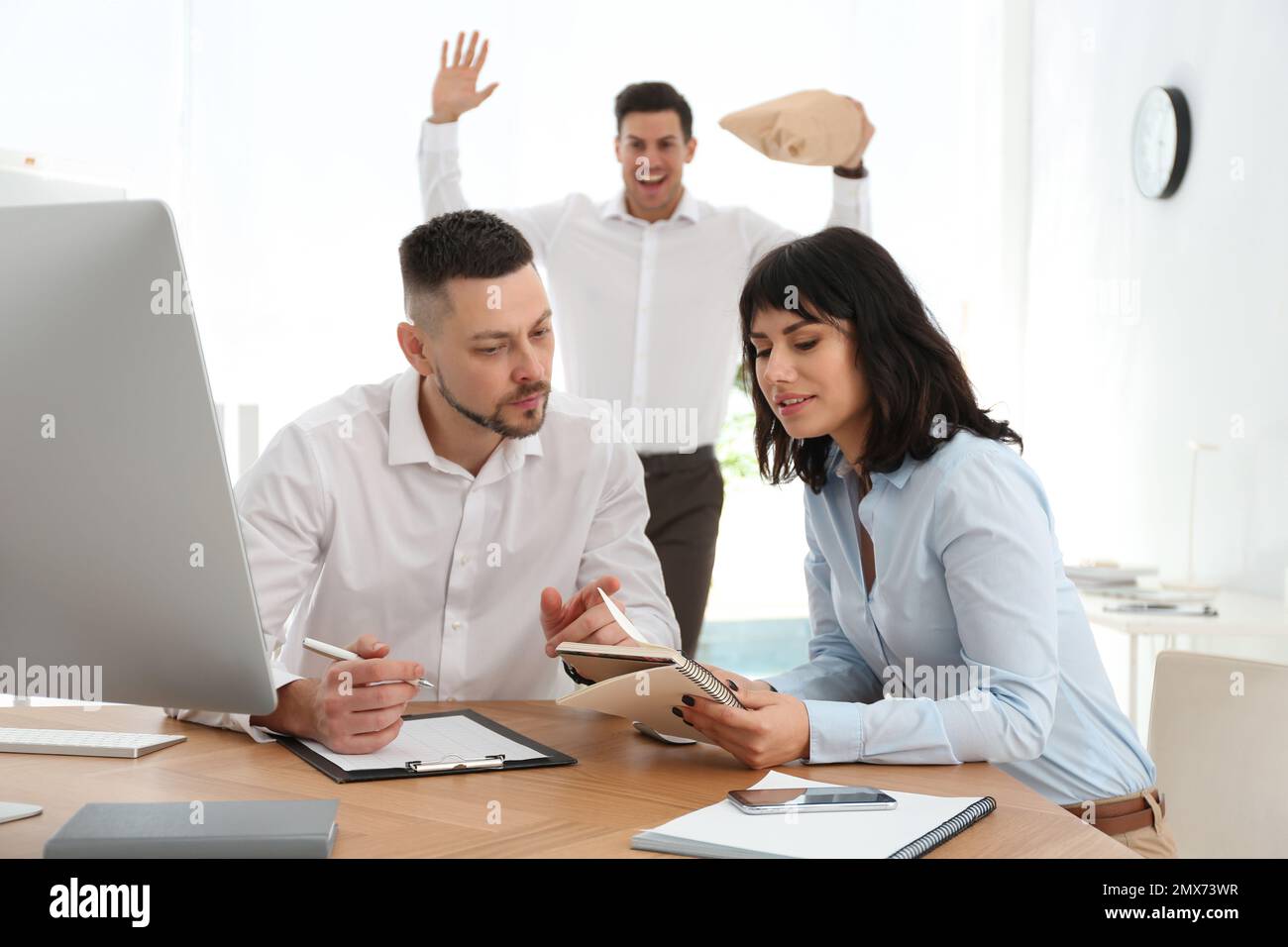 Man popping paper bag behind his colleagues in office. April fool's day ...