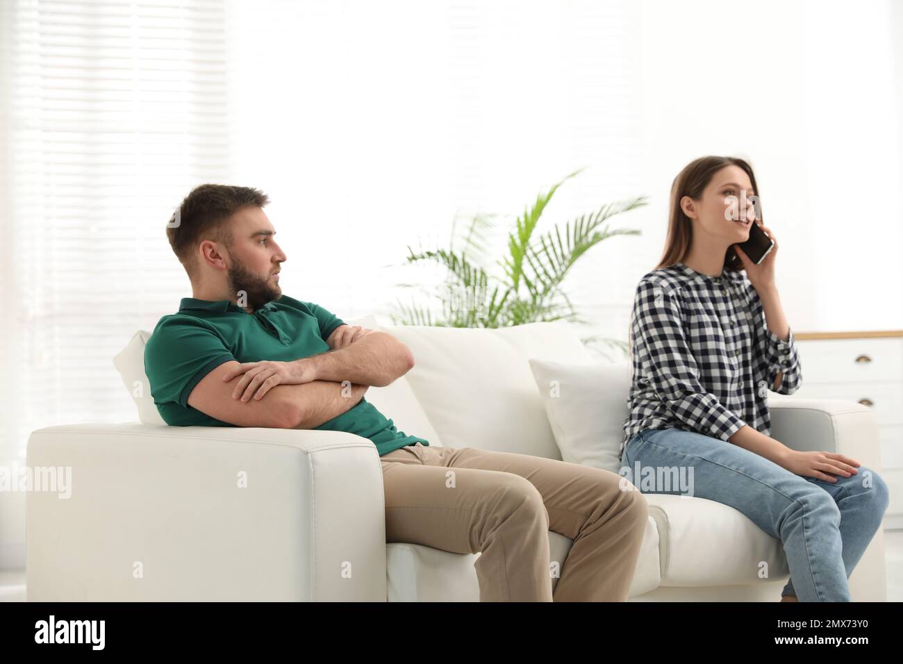 Young woman with smartphone ignoring her boyfriend at home ...