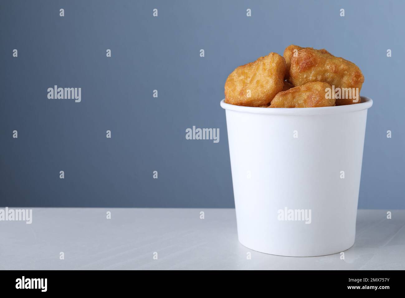 Bucket with tasty chicken nuggets on light grey table against blue ...