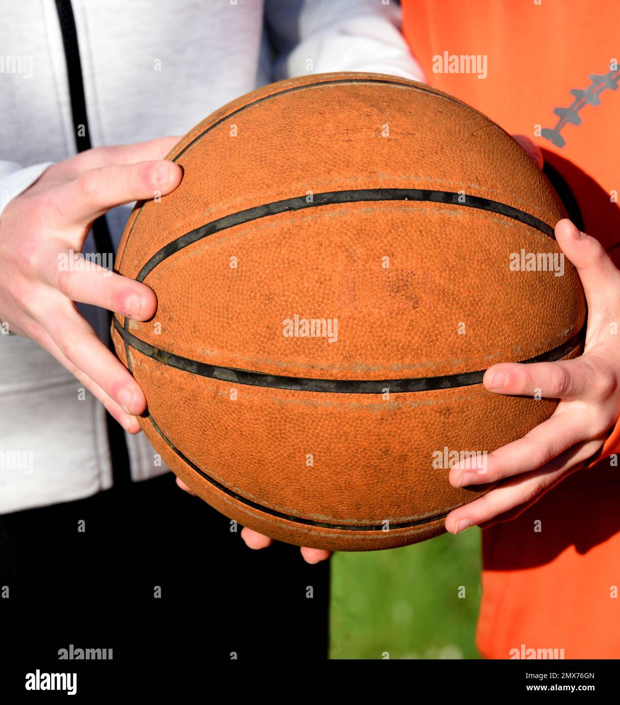 Two young teens share turns with the basketball. They are outdoors ...