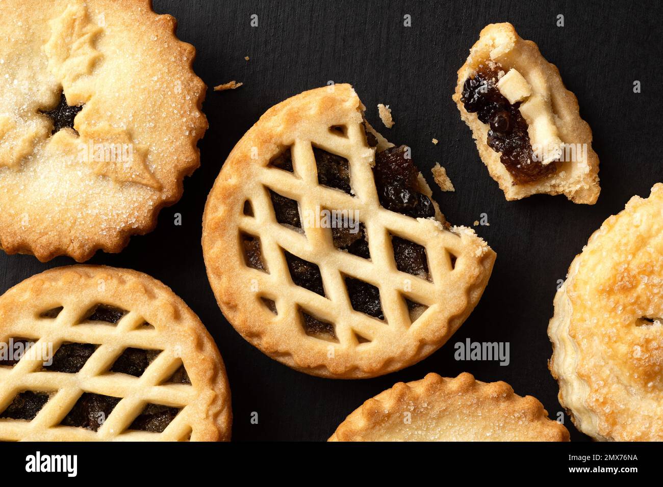 All butter mince pies on black surface. One broken with fruit filling ...