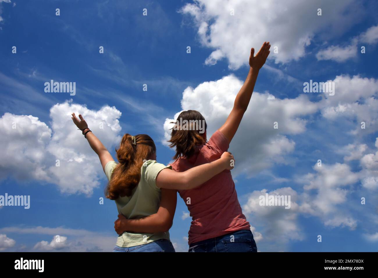 Two young teenage girls hold their arms wide and embrace and blue sky ...