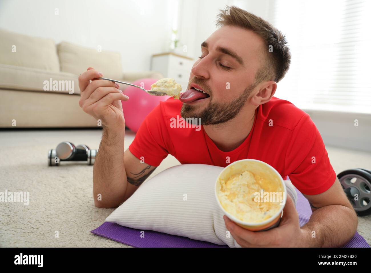 Lazy young man eating ice cream instead of training at home Stock Photo ...