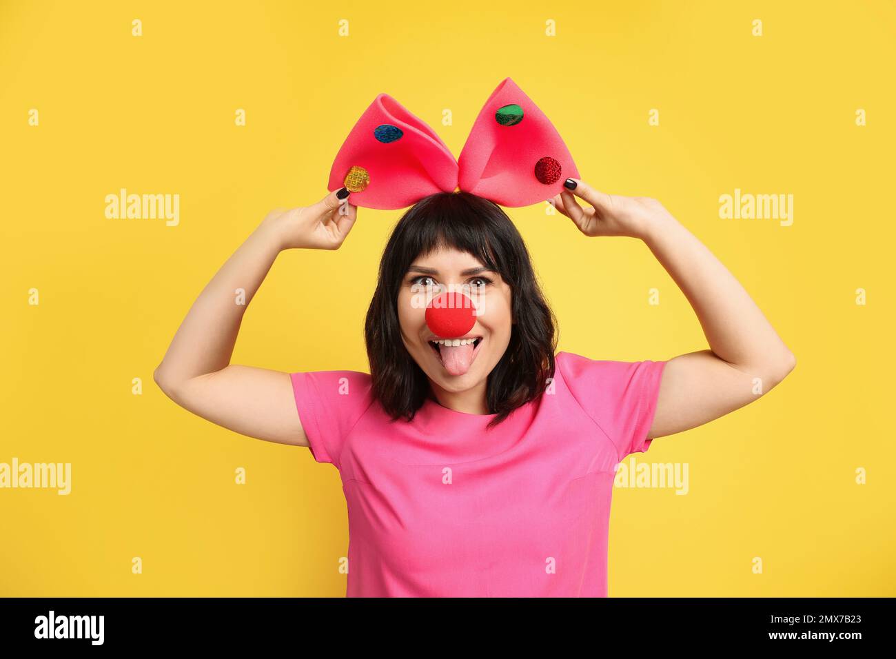 Funny woman with large bow and clown nose on yellow background. April ...