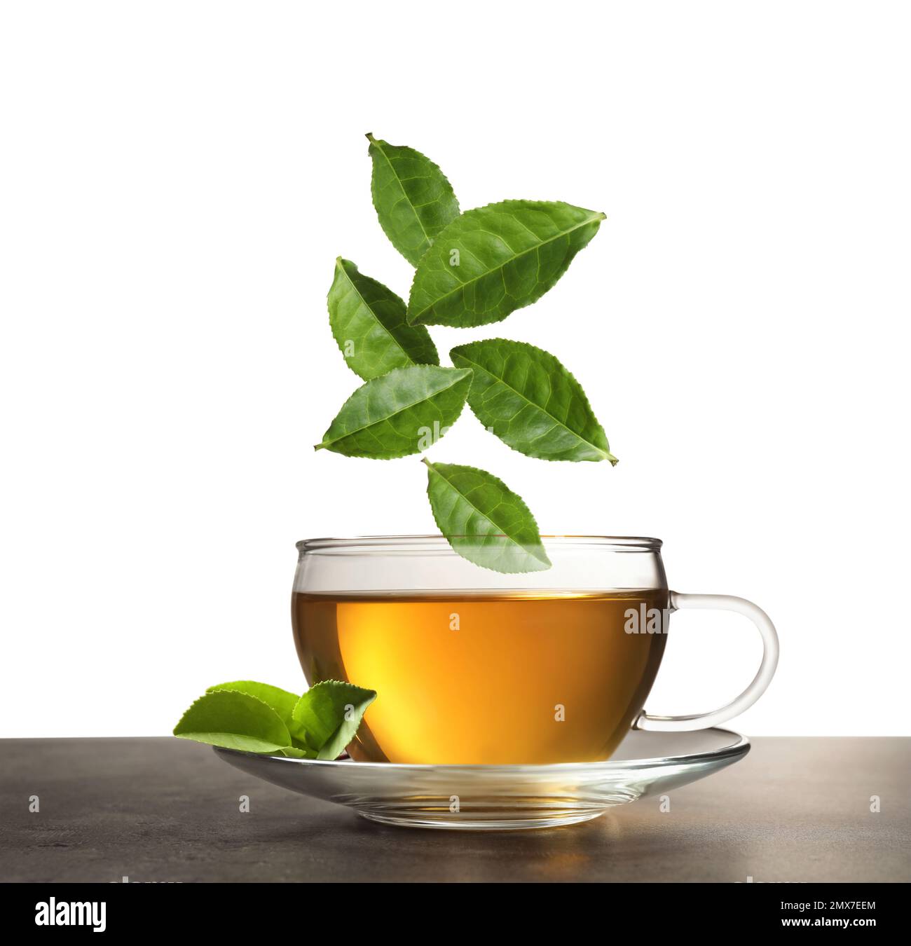 Green leaves falling into cup of tea on table against white background ...
