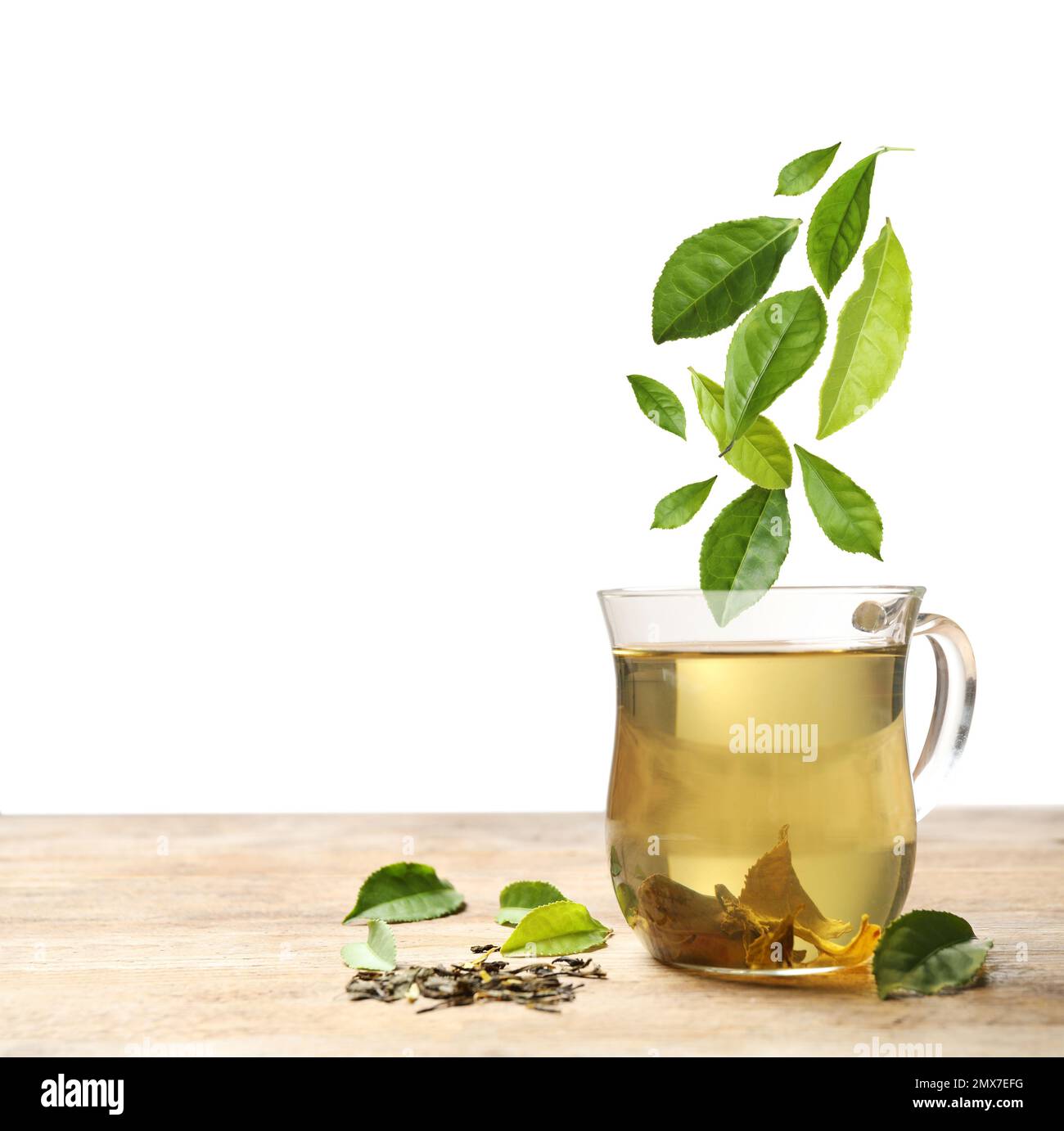 Green leaves falling into cup of tea on table against white background ...