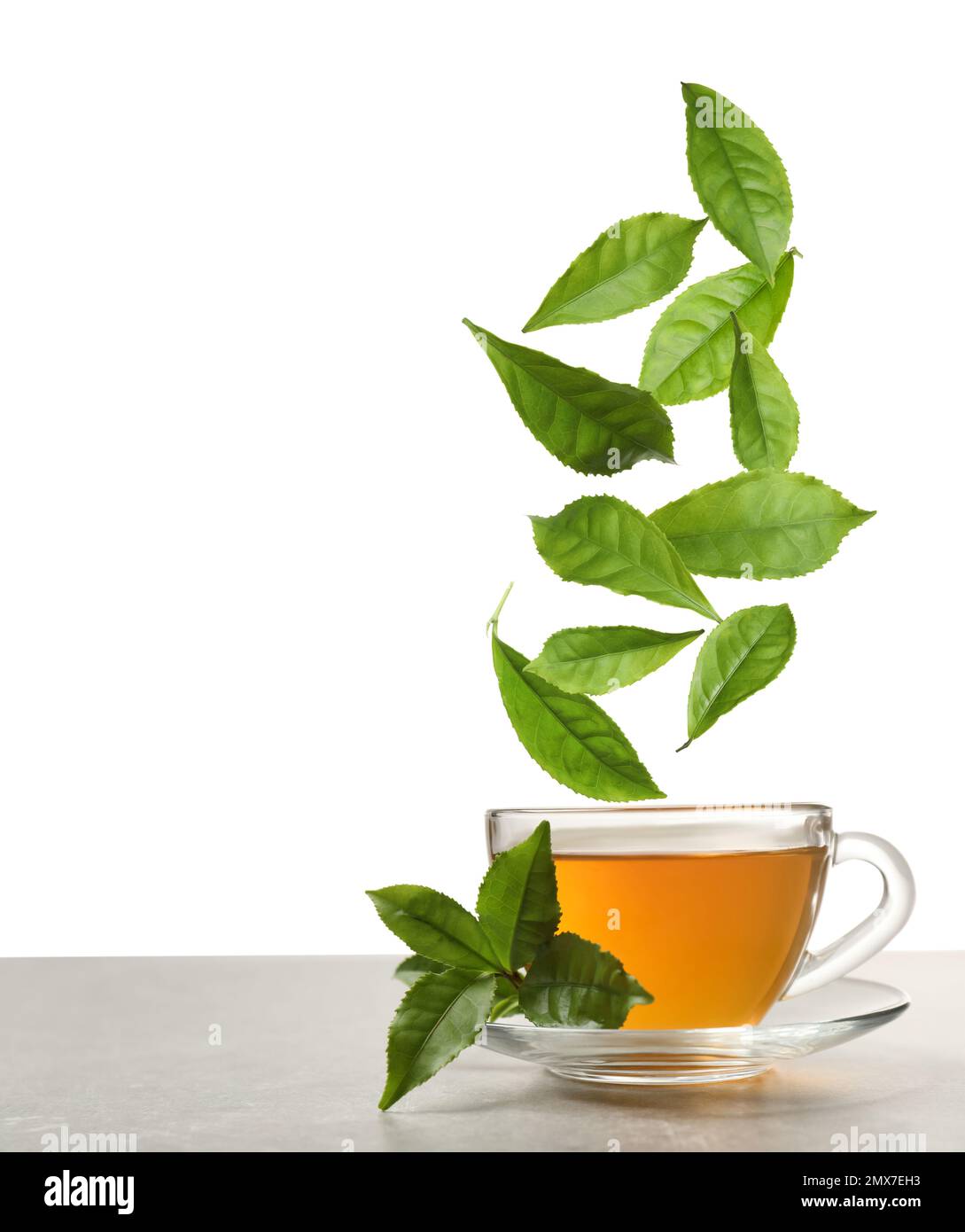 Green leaves falling into cup of tea on table against white background ...