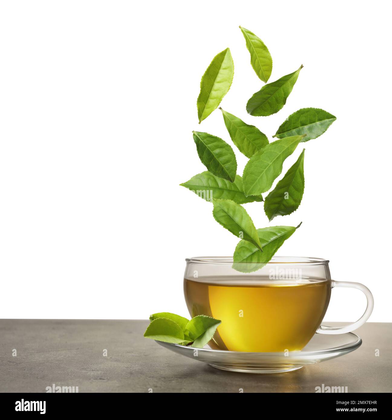 Green leaves falling into cup of tea on table against white background ...