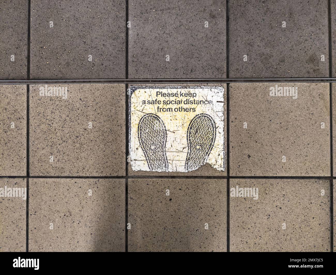A worn social distancing sticker on the floor of a platform in the ...