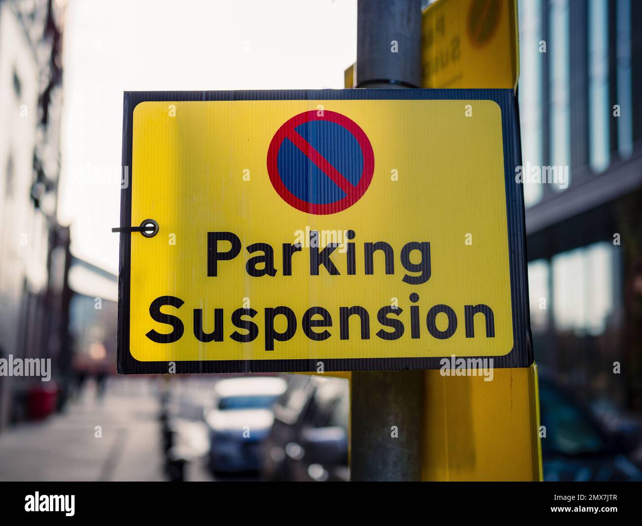 a bright yellow parking suspension sign by the road side attached to ...