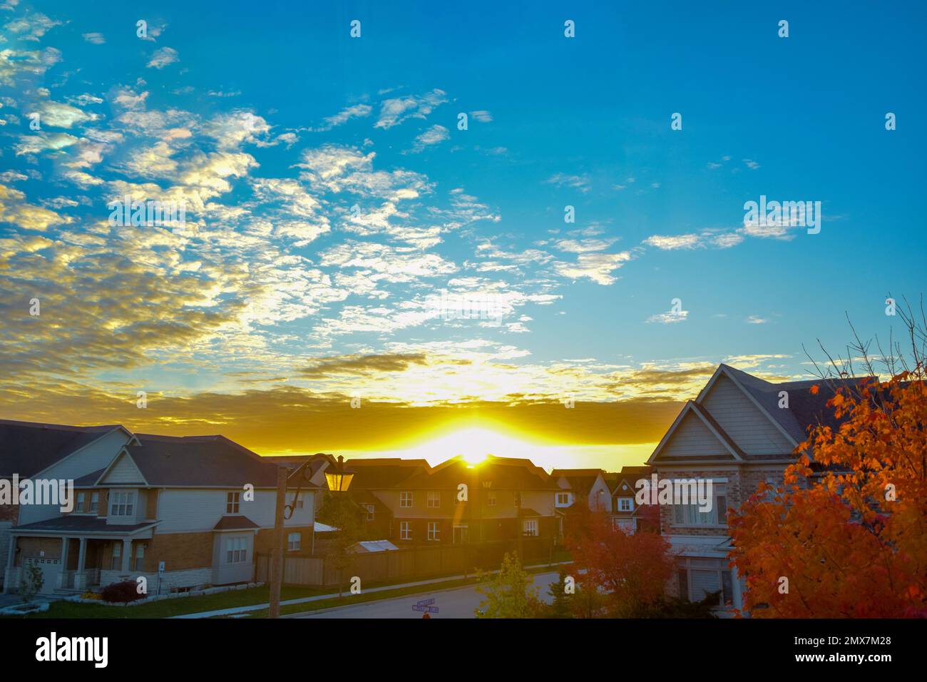 The sun rises from behind the roofs on the autumn street, illuminating ...