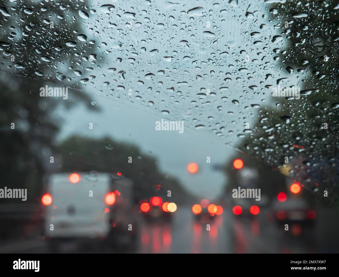 Closeup of raindrops on a windshield, and blurry road traffic with cars ...
