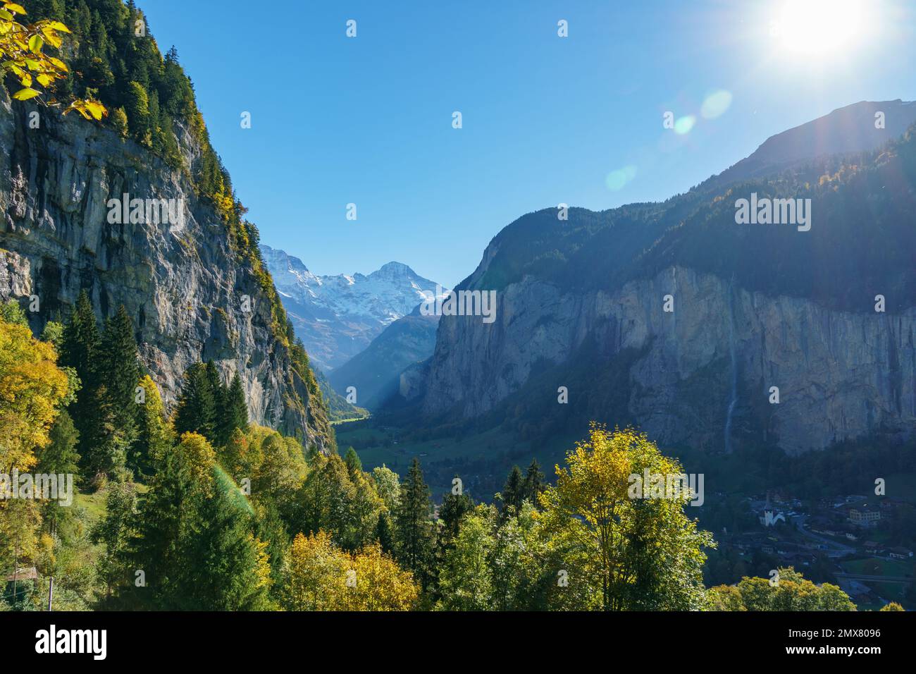 Steep alpine mountains descend to a shadowy valley and the town of ...