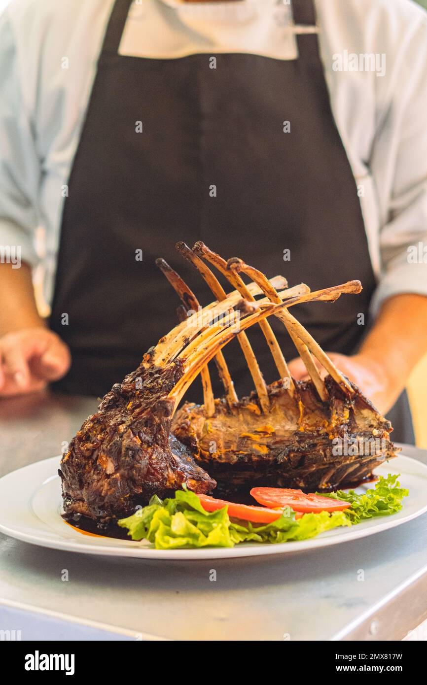 Crop anonymous cook in white uniform cutting meat from ribs while ...