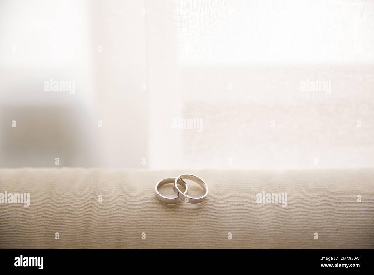 Elegant wedding rings placed on beige surface in light room with ...