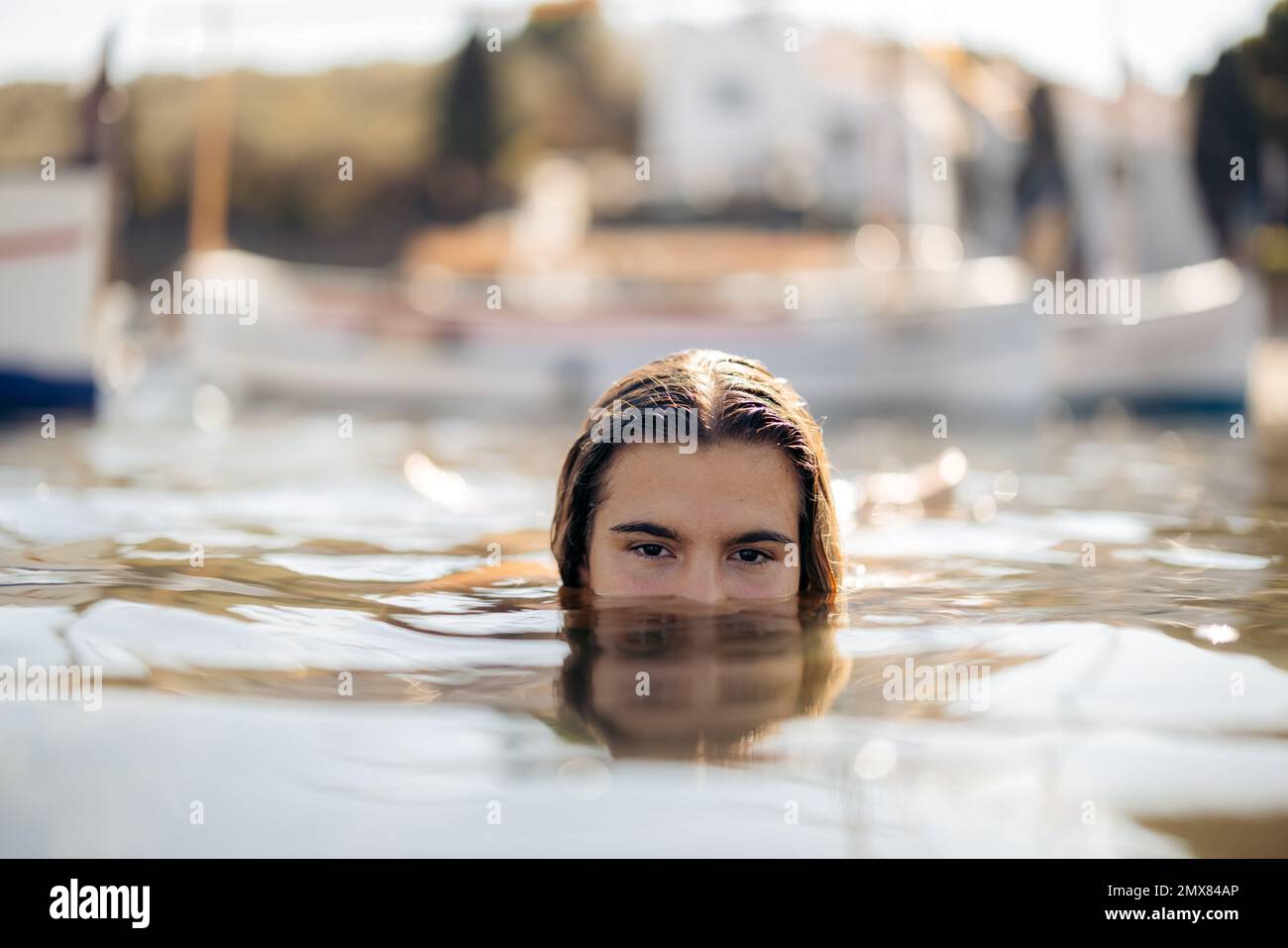 Calm female looking at camera and dipping in sea water while swimming ...