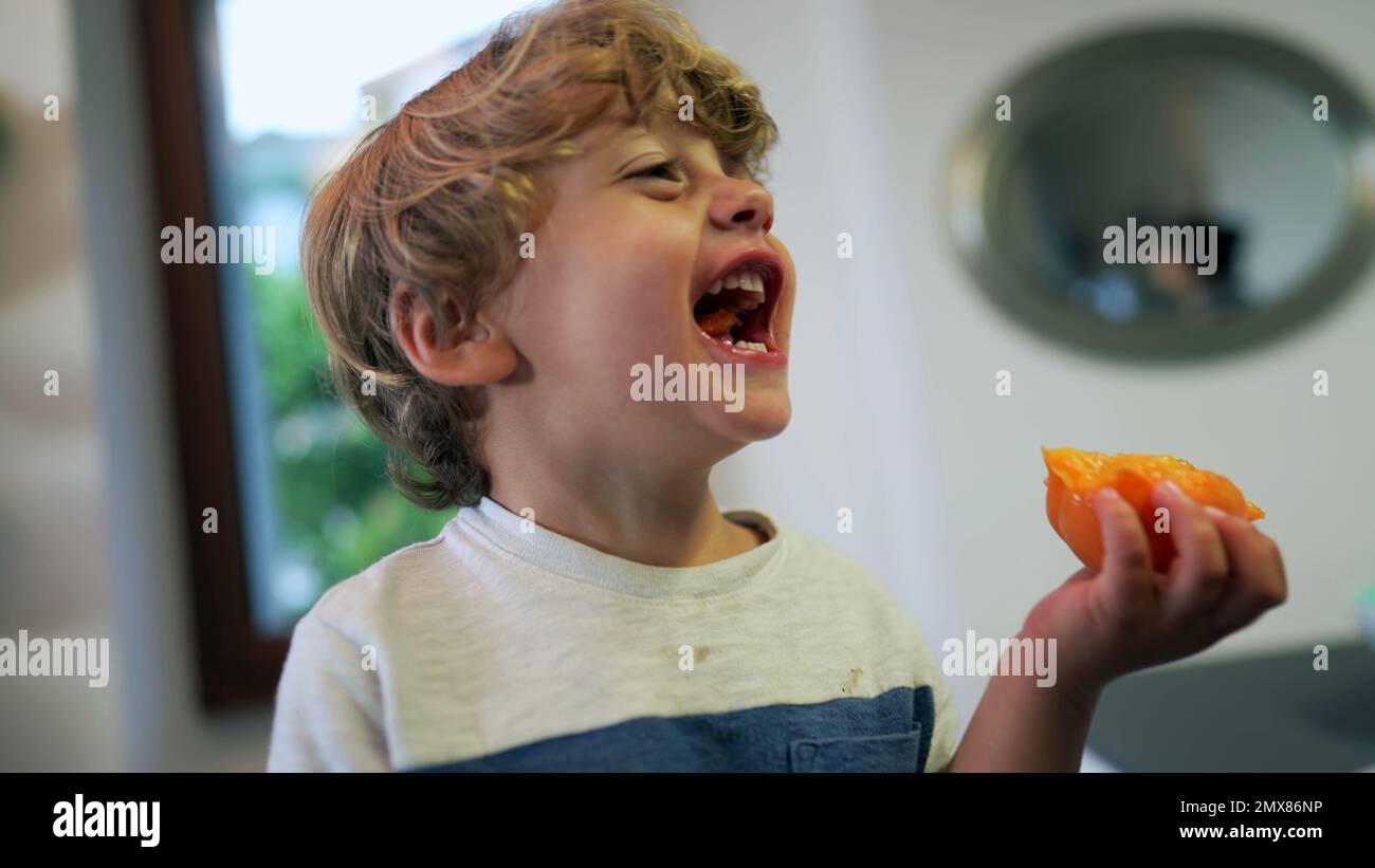 Happy child eating healthy fruit indoors for breakfast. One little boy ...