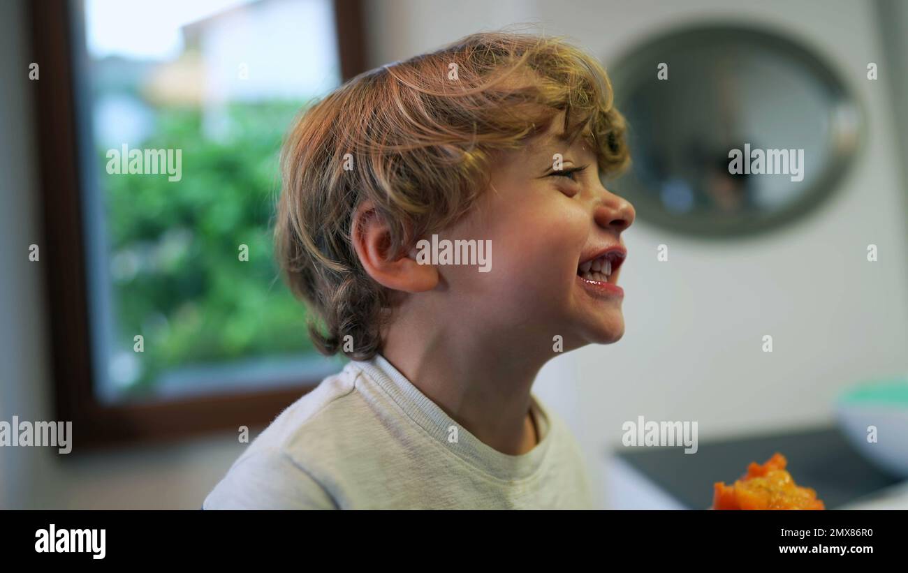 Happy child eating healthy fruit indoors for breakfast. One little boy ...
