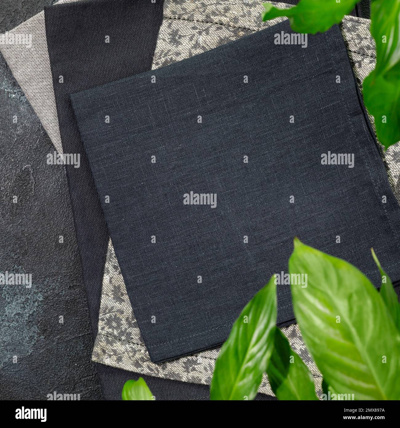 Folded black napkins on black background with green leaves. Eco ...