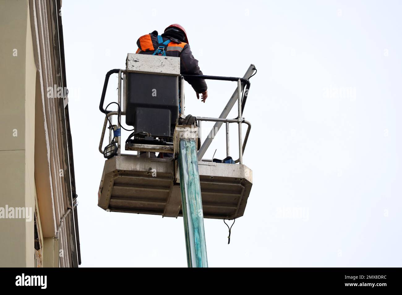 Worker in hydraulic lifting ramp repairs the building facade. Builder ...